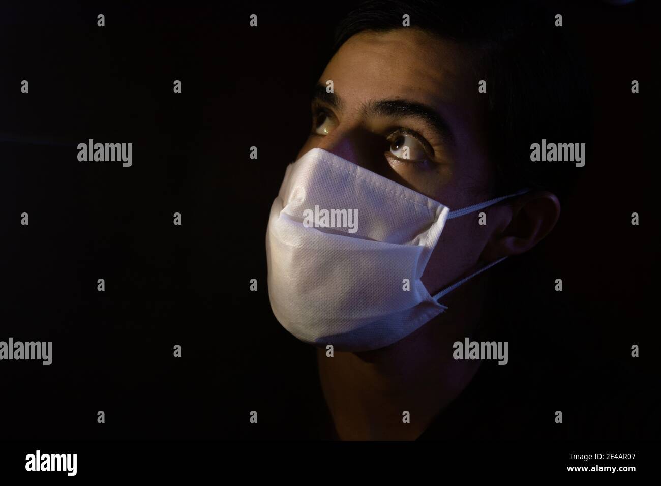 Portrait of a young man with a disposable white face mask looking up ...