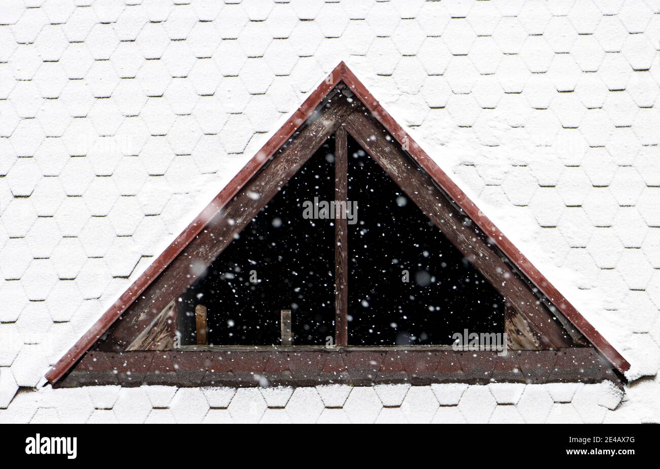 The dormer without glass in the windows on the snowy roof. Falling snow ...