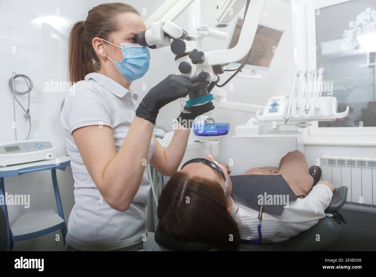 Female dentist operating dental microscope, treating teeth of patient ...
