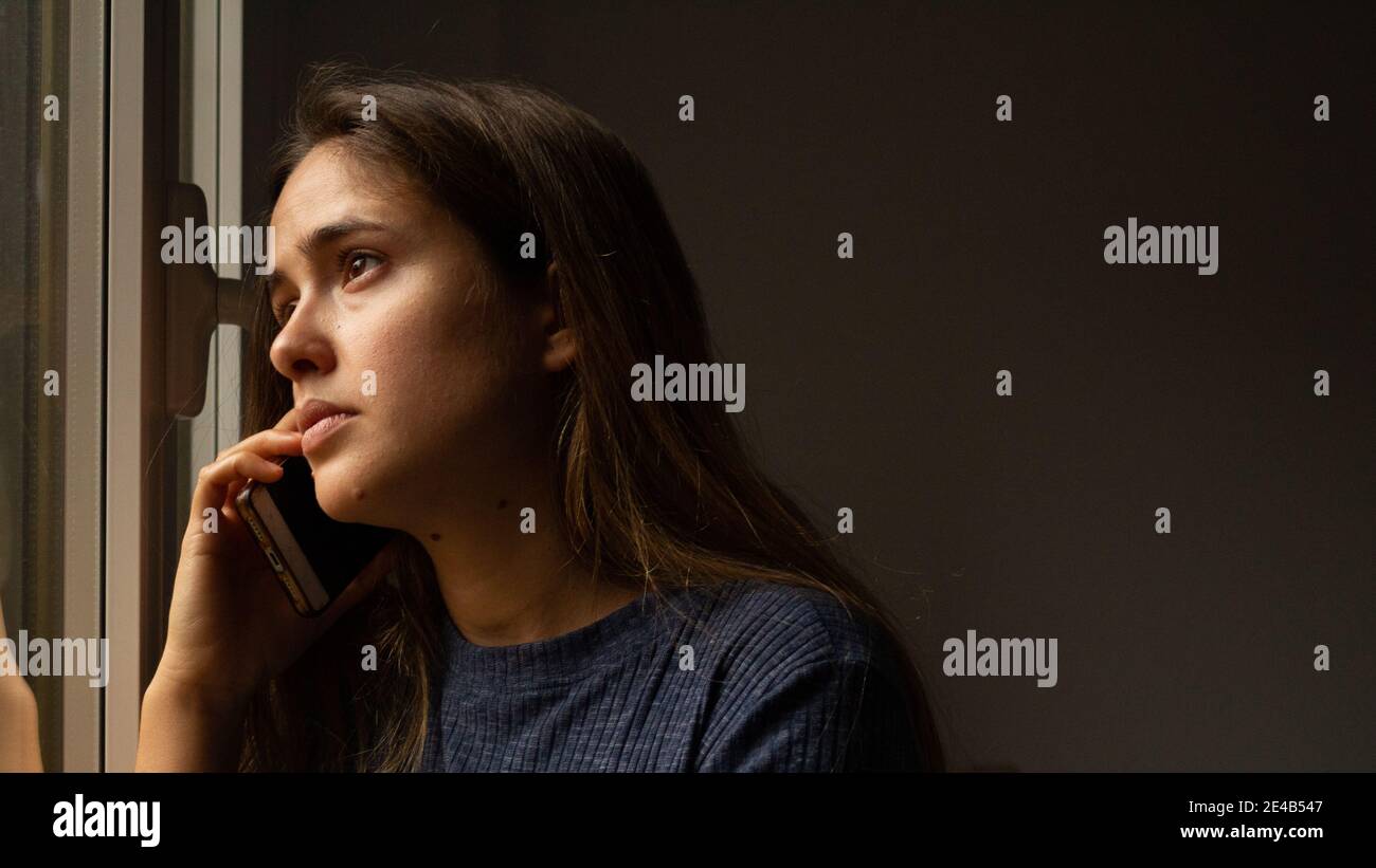 Young European female with a sad facial expression talking on a phone ...