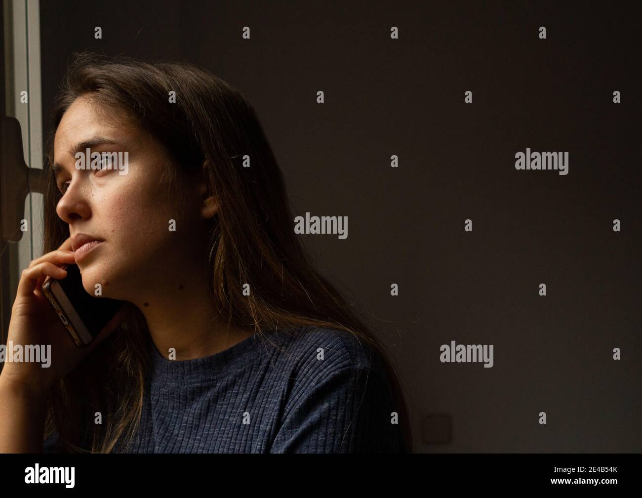Young European female with a sad facial expression talking on a phone ...