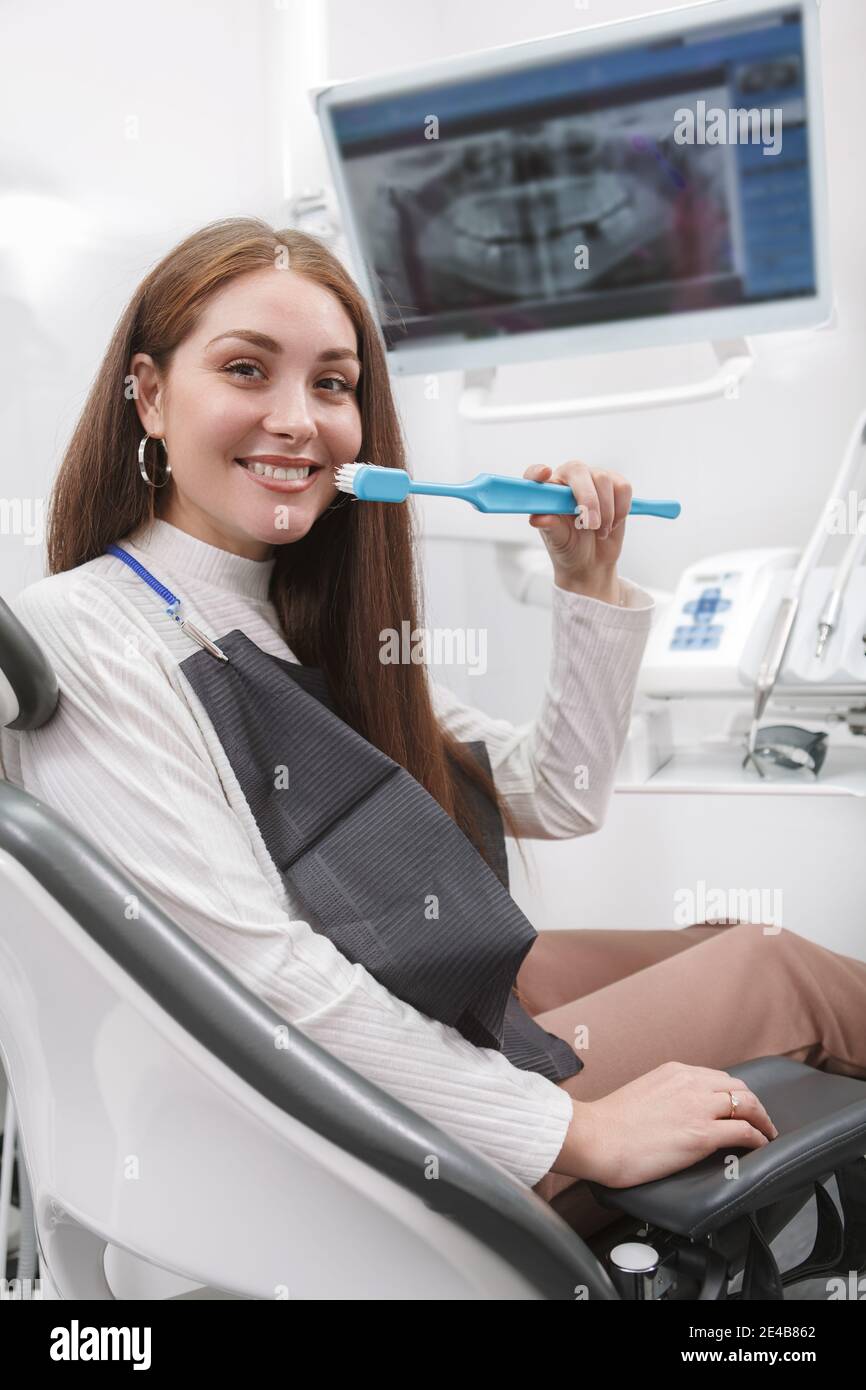 Vertical portrait of a happy woman sitting in dental chair holding big ...