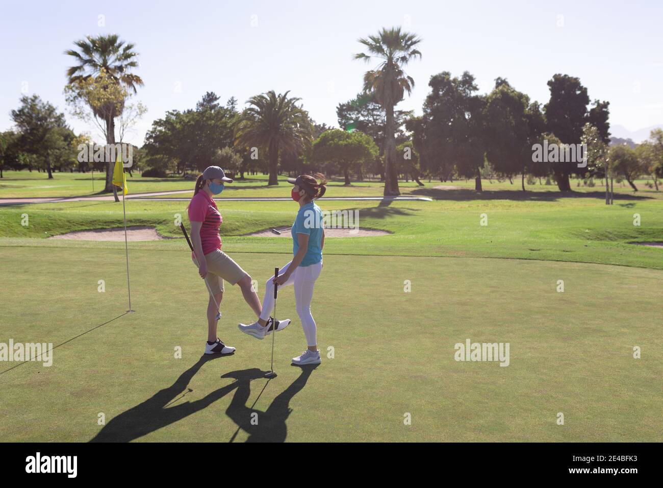 Two caucasian women wearing face masks greeting on golf course by ...