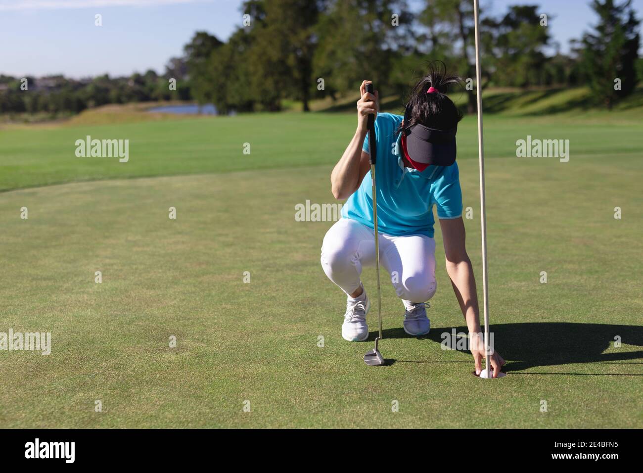 Caucasian woman wearing face mask taking ball from hole on golf course ...