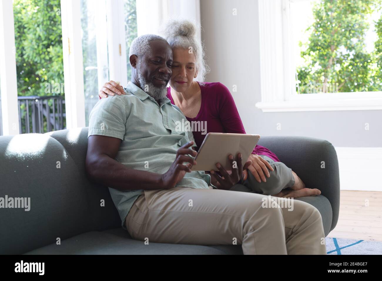 Senior mixed race couple sitting on couch looking at digital tablet ...