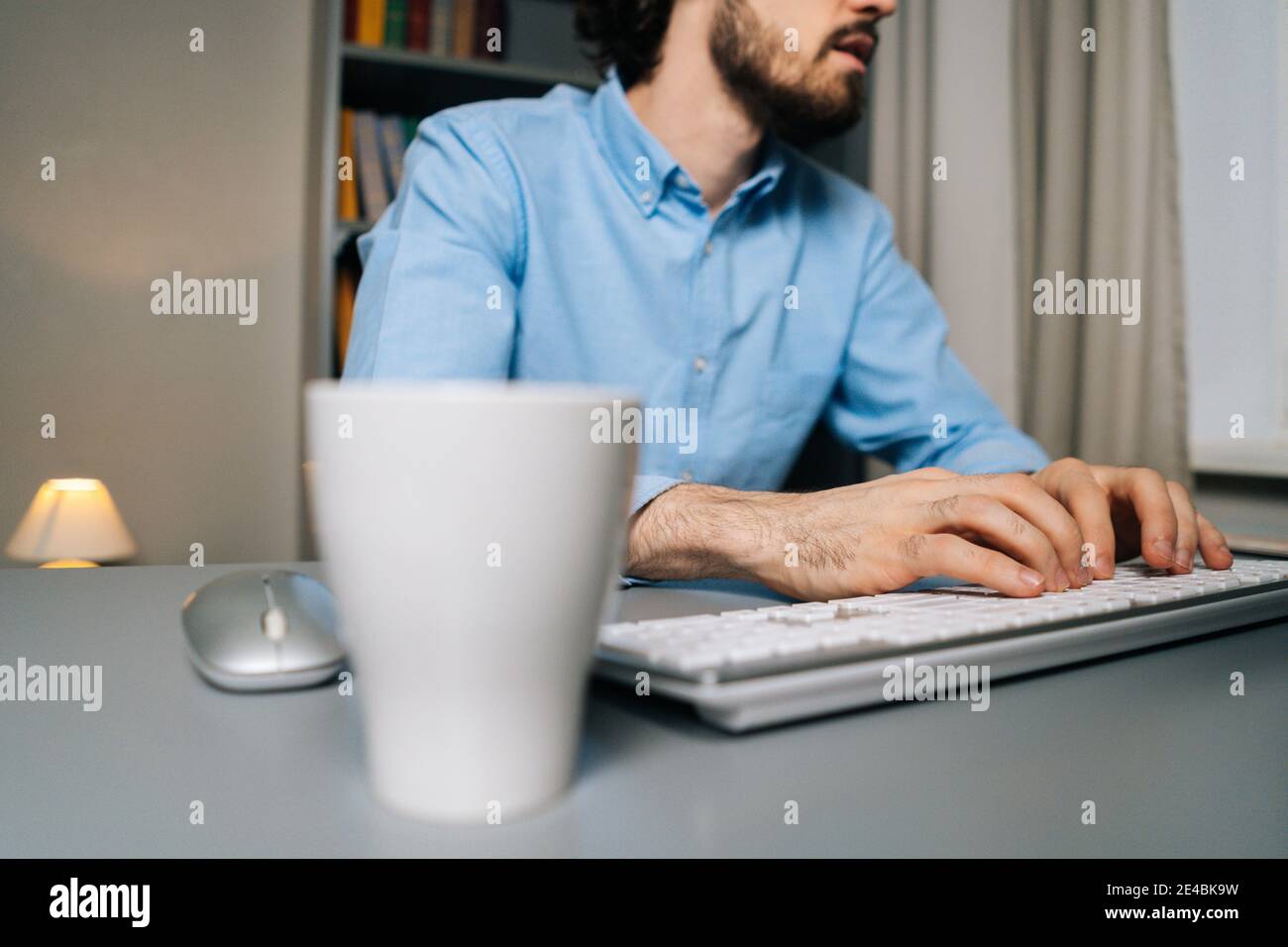 Close-up of unrecognizable man using computer and typing online message on wireless keyboard ...