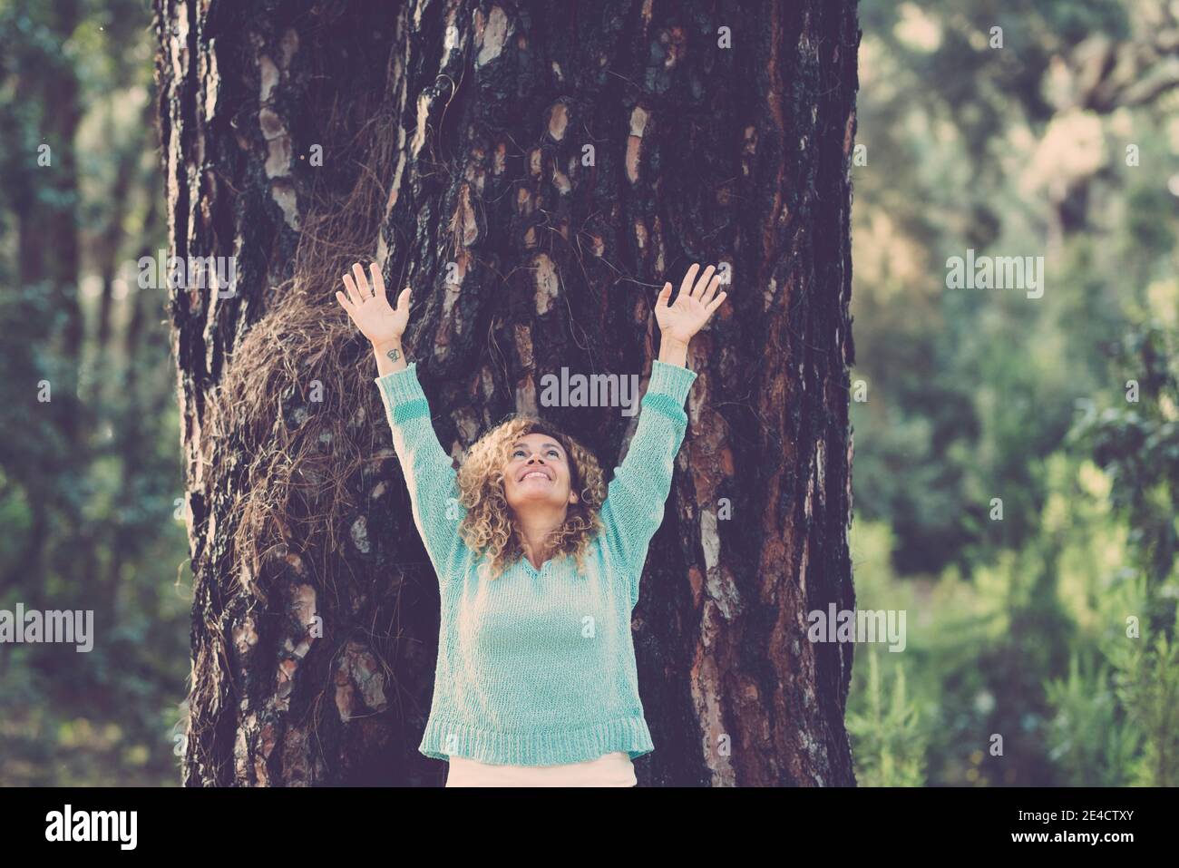 Cheerful nice pretty woman standing with big tree trunk in background ...