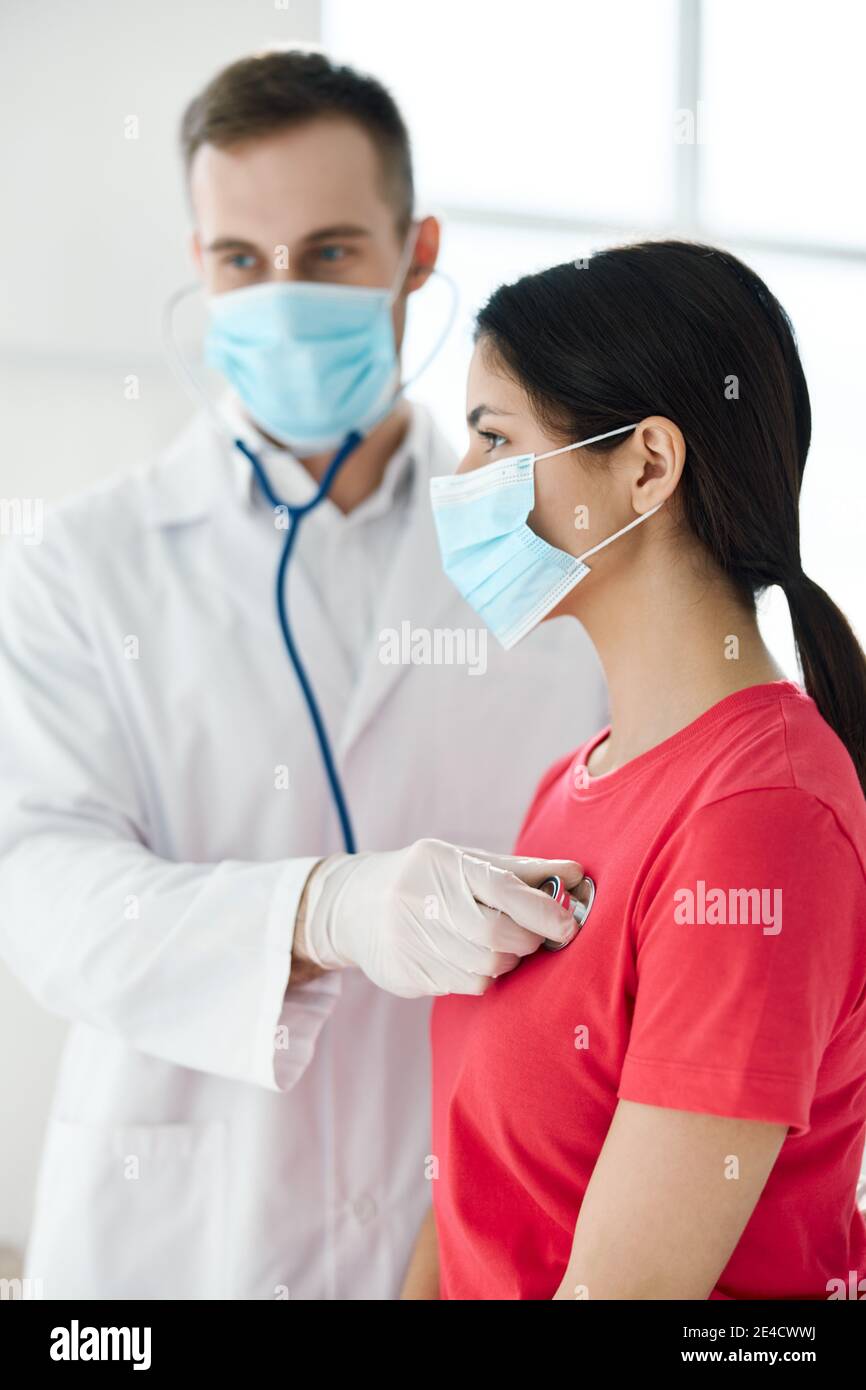 doctor with a stethoscope examines a patient wearing a medical mask ...