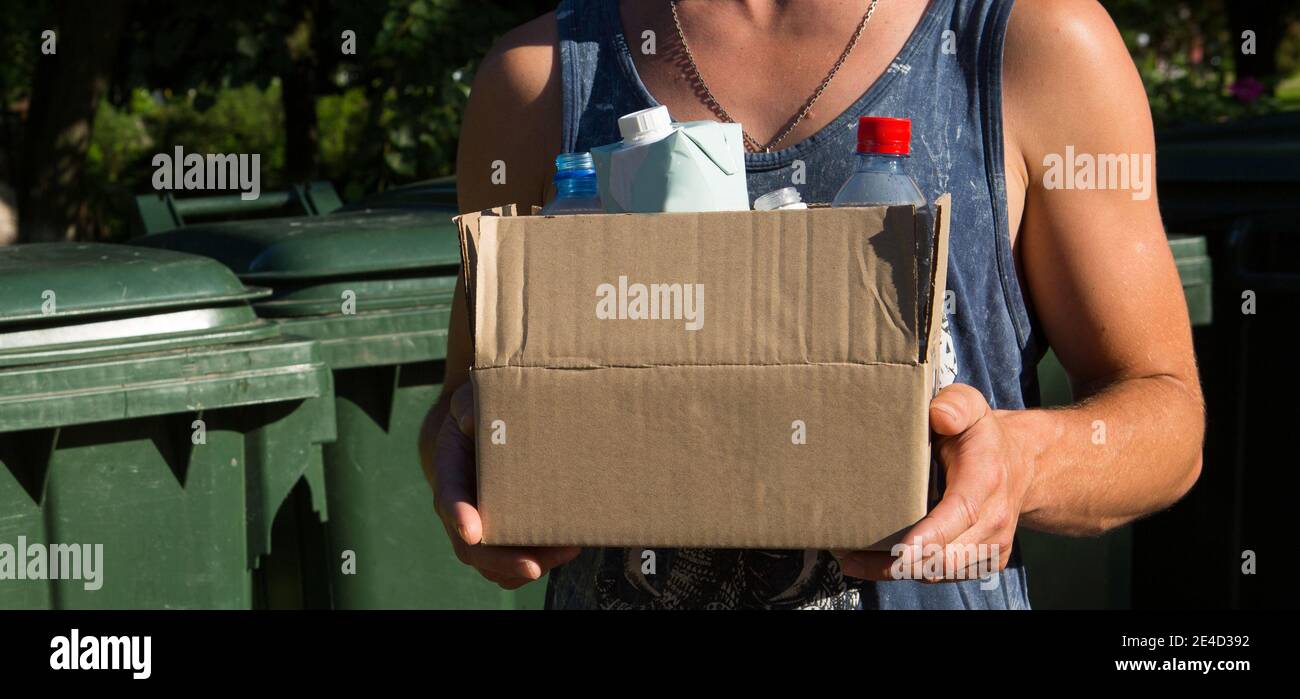 A cardboard box with garbage in the hands of a man near containers for ...