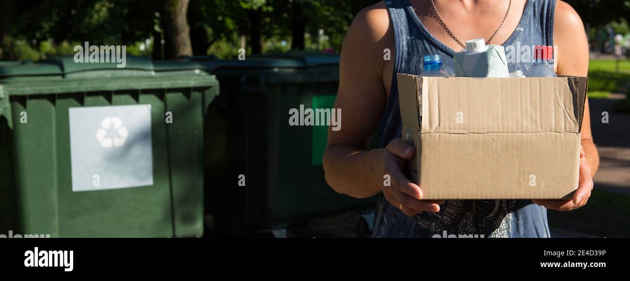 A cardboard box with garbage in the hands of a man near containers for ...