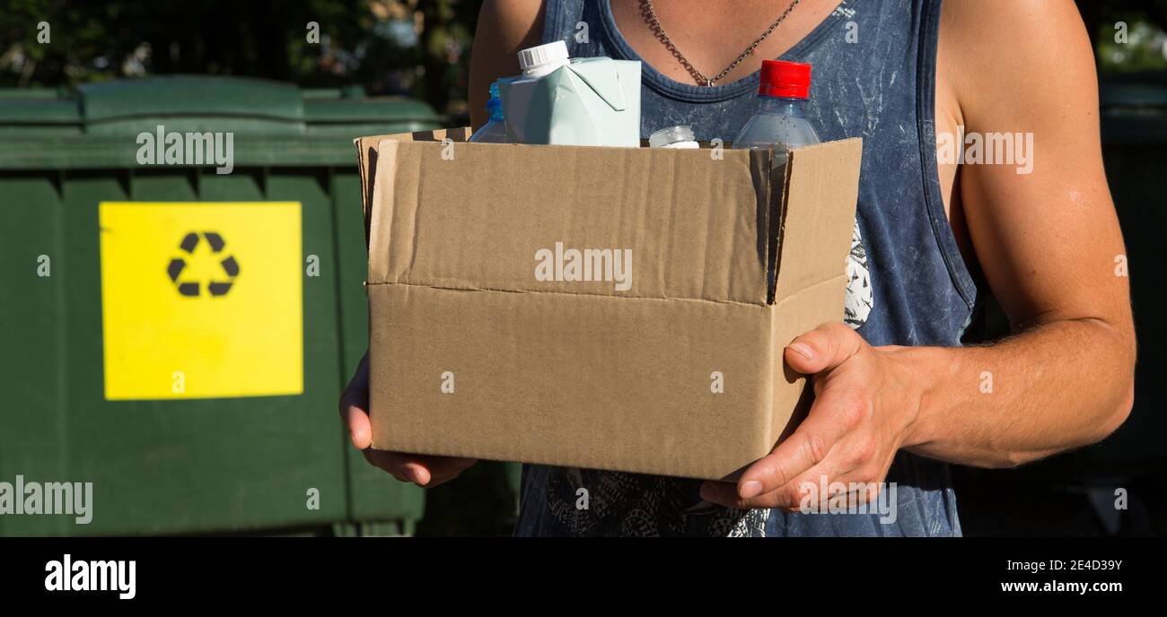 A cardboard box with garbage in the hands of a man near containers for ...