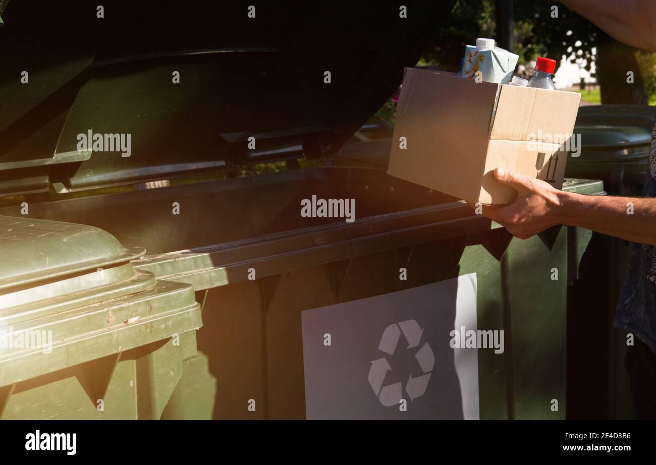 A cardboard box with garbage in the hands of a man near containers for ...