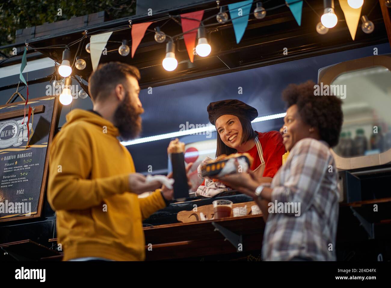 female employee socializing with multiethnic couple eating sandwiches ...