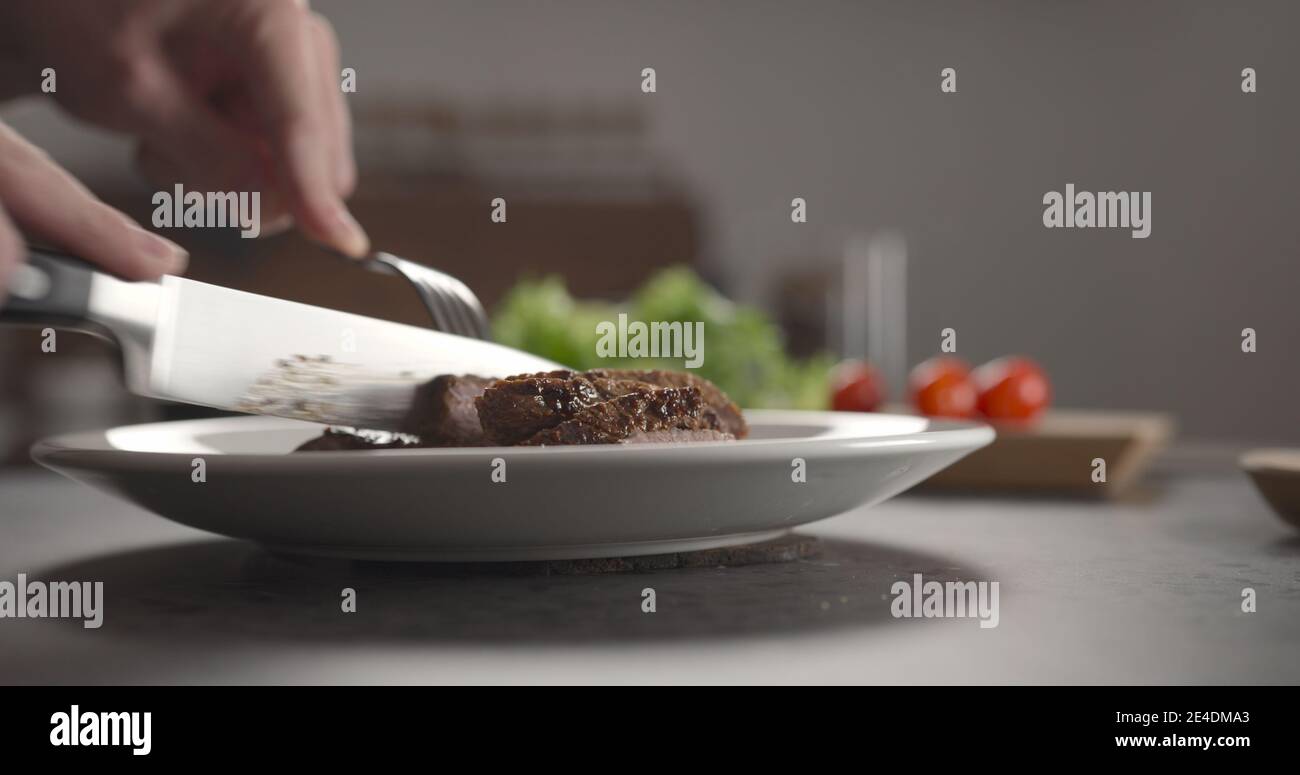 Man slicing beef steak on white plate on kitchen countertop, wide photo ...