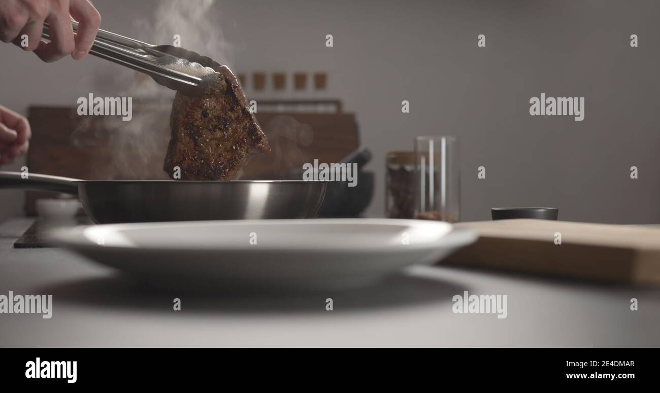 man put whole beef steak on black plate on concrete countertop, wide ...