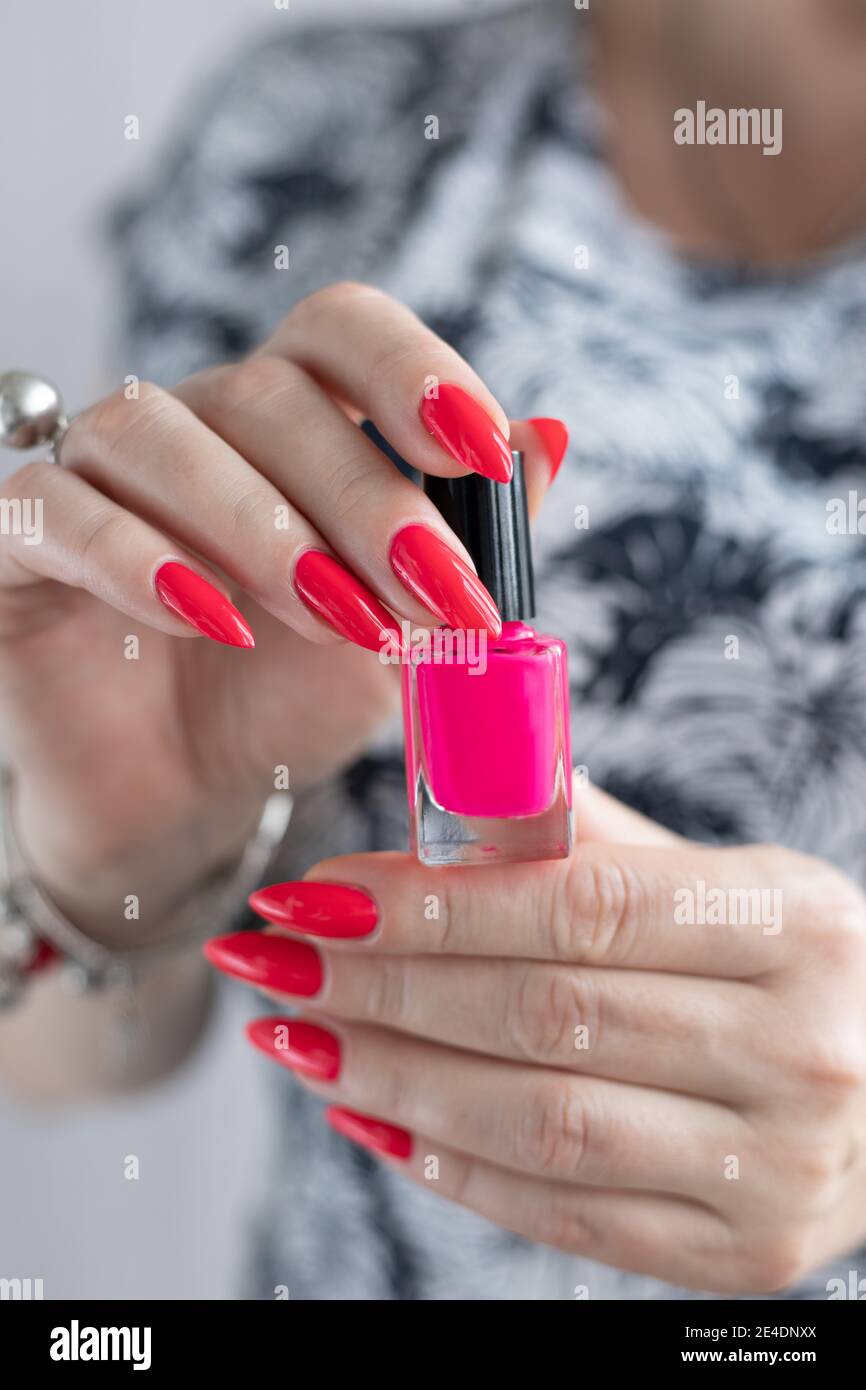 Woman's hands with long nails and a bottle of red orange nail polish ...