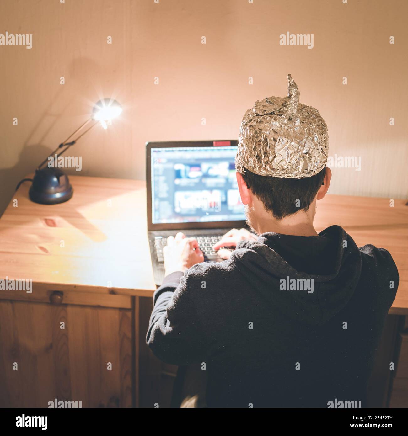 Young man with aluminum cap is sitting in the dark basement in front of ...