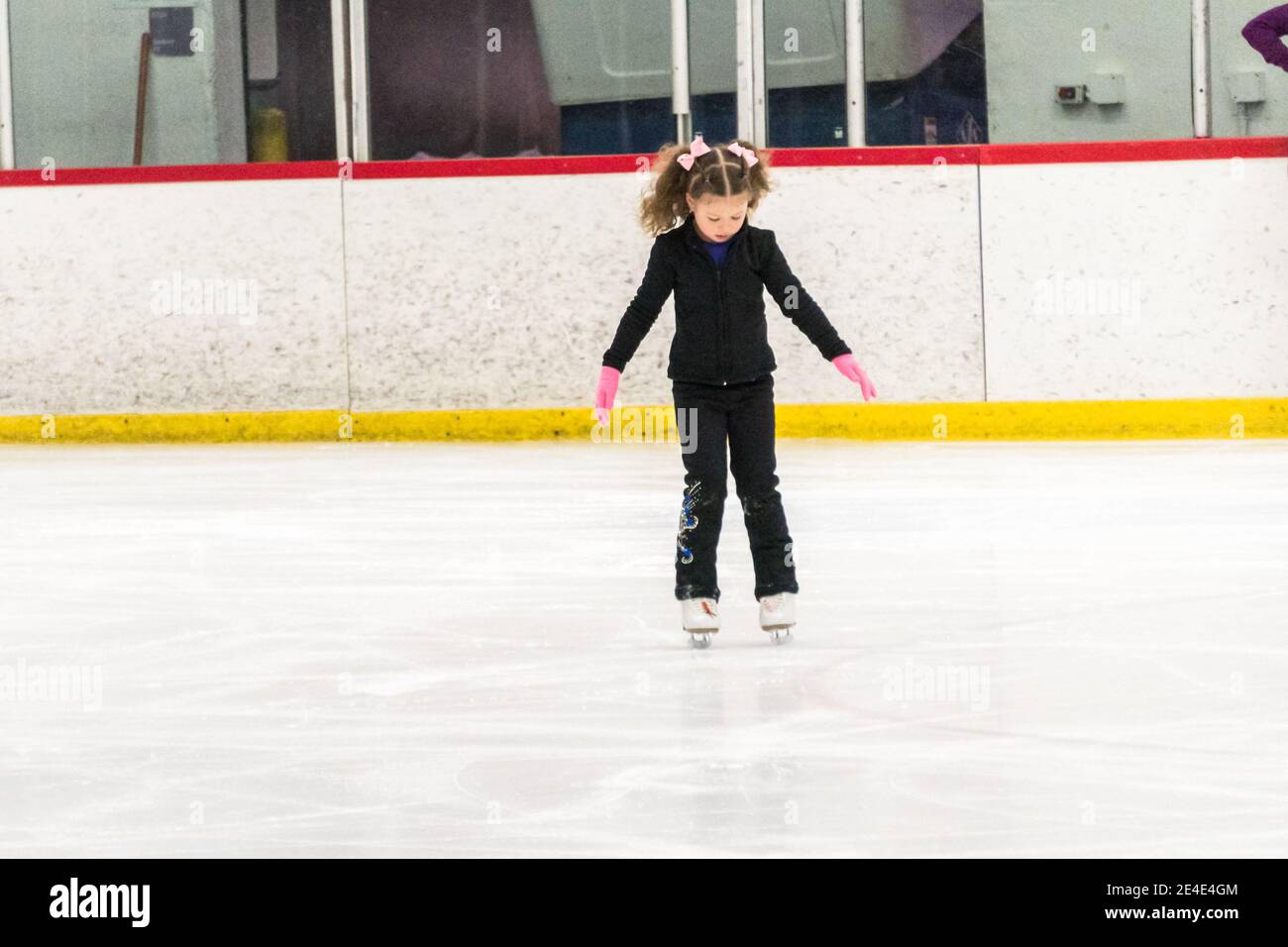 Little girl practicing figure skating moves on the indoor ice rink ...