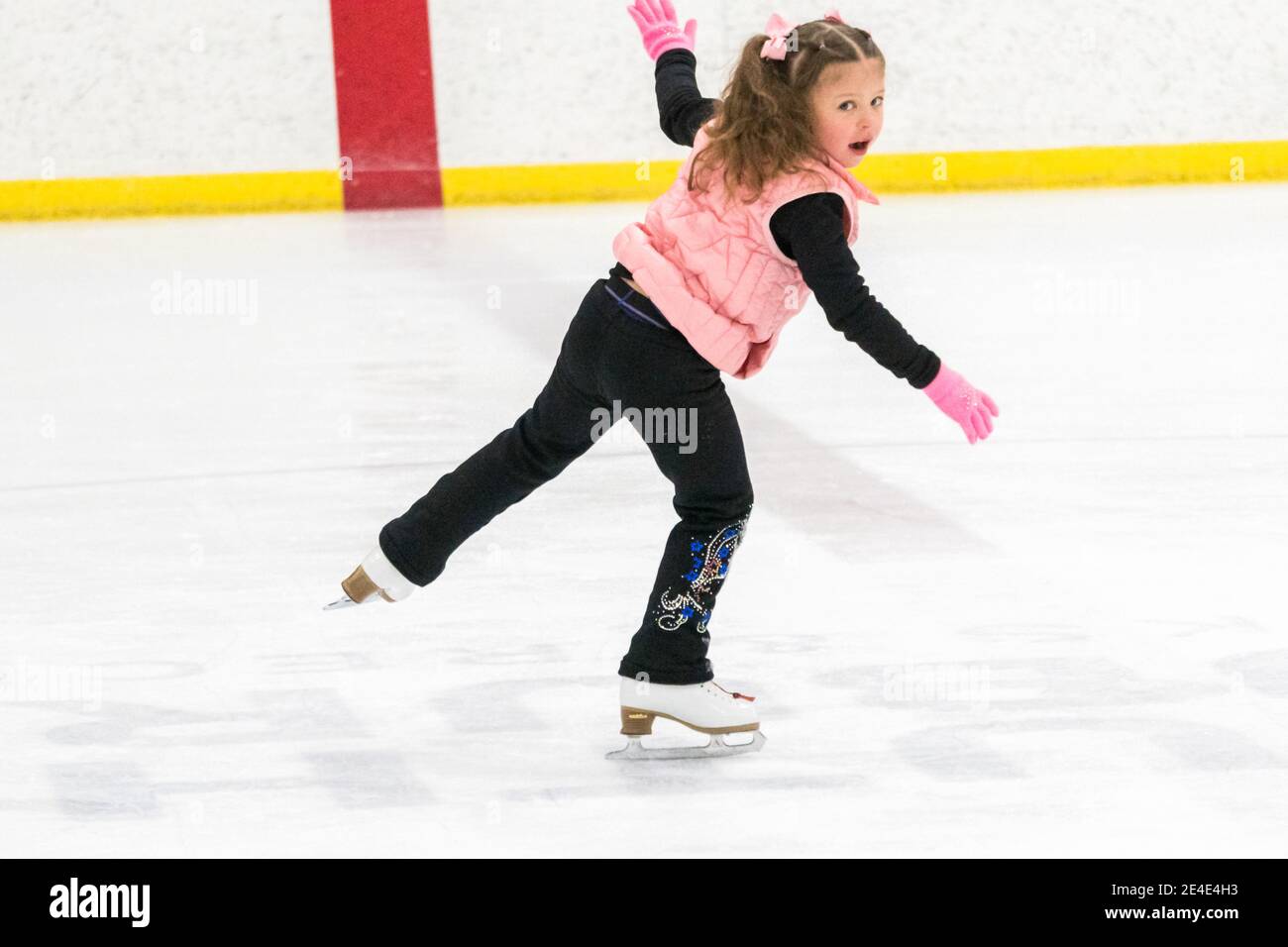 Little girl practicing figure skating moves on the indoor ice rink ...
