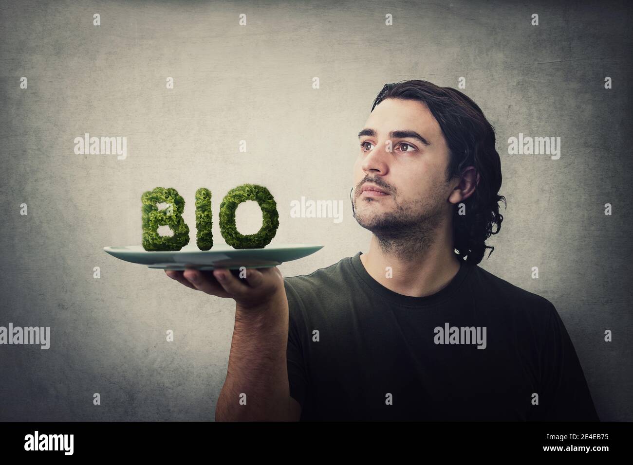 Young man waiter holding dish plate with Bio text made of green salad ...