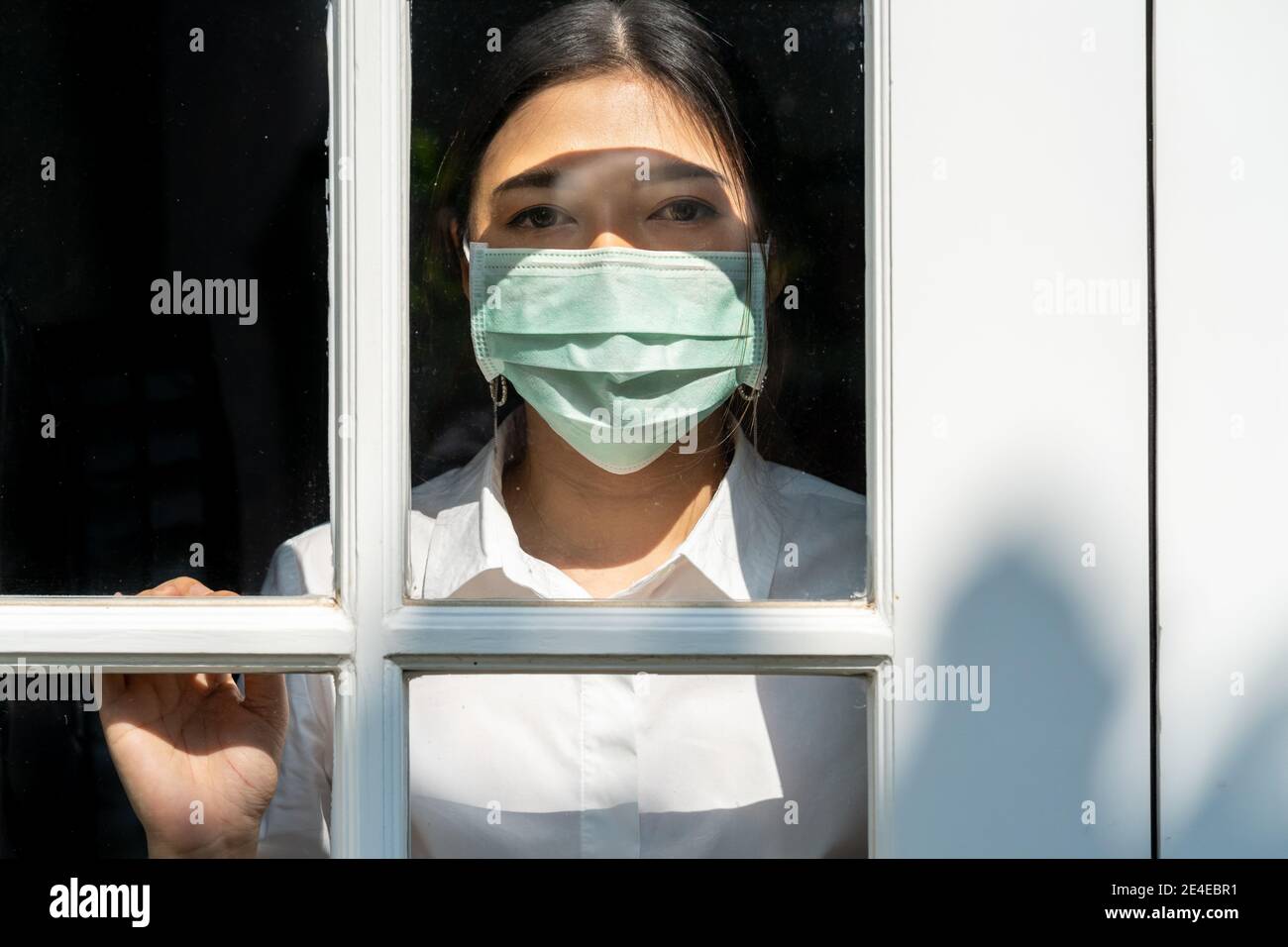 Young woman wearing surgical mask staying inside her home looking out ...