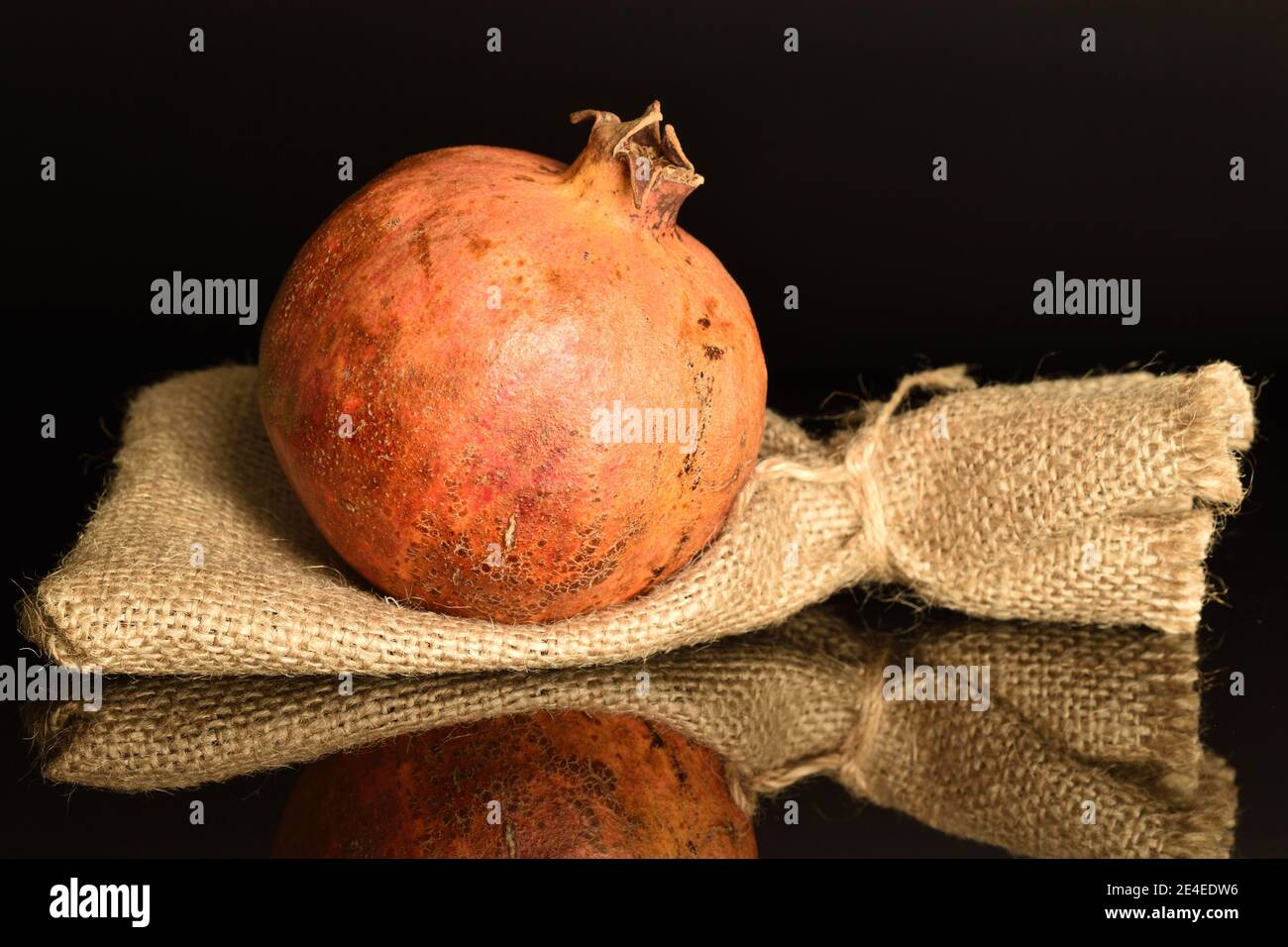 One juicy pomegranate with a jute bag, close-up, on a black background ...