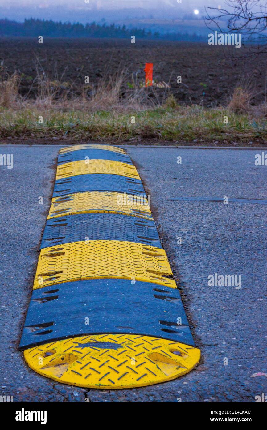 Navy blue and yellow speed bump on a small country road with a field in ...