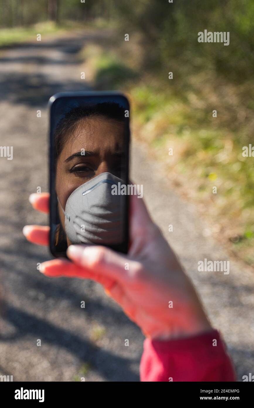 Vertical shot of a woman wearing a medical mask reflected in a mobile ...