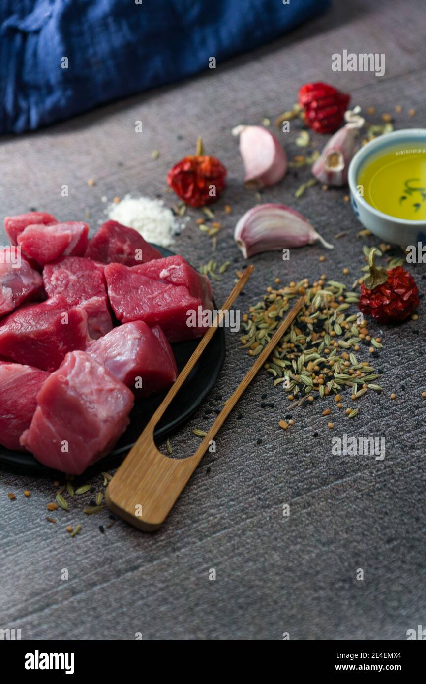 Vertical shot of raw cut meat, garlic cloves, dried pepper, oil on the ...