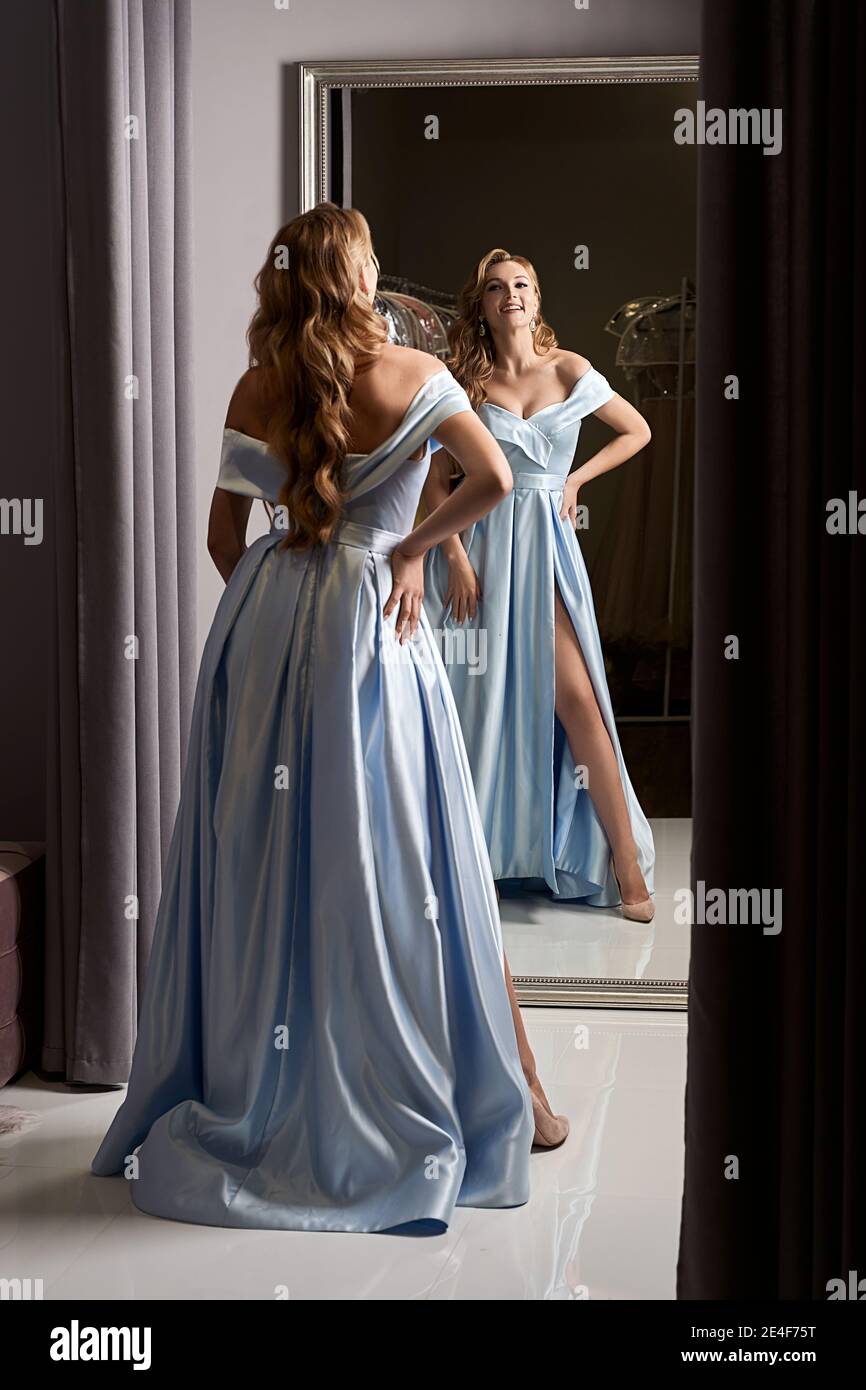 Young beautiful blonde girl wearing an off-the-shoulder full-length sky blue satin slit prom ...