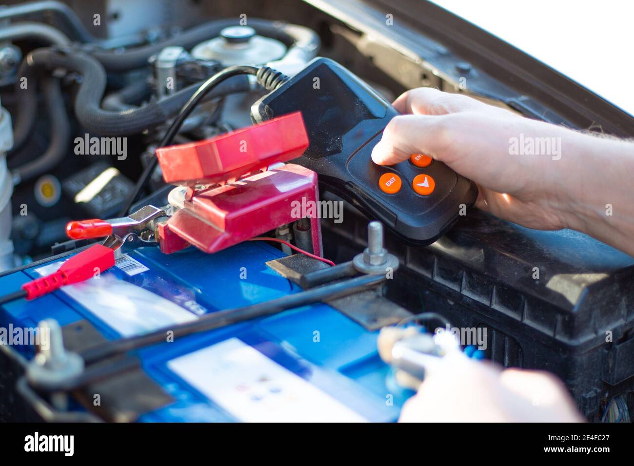 a car mechanic under the hood of a car diagnoses a car battery with a ...