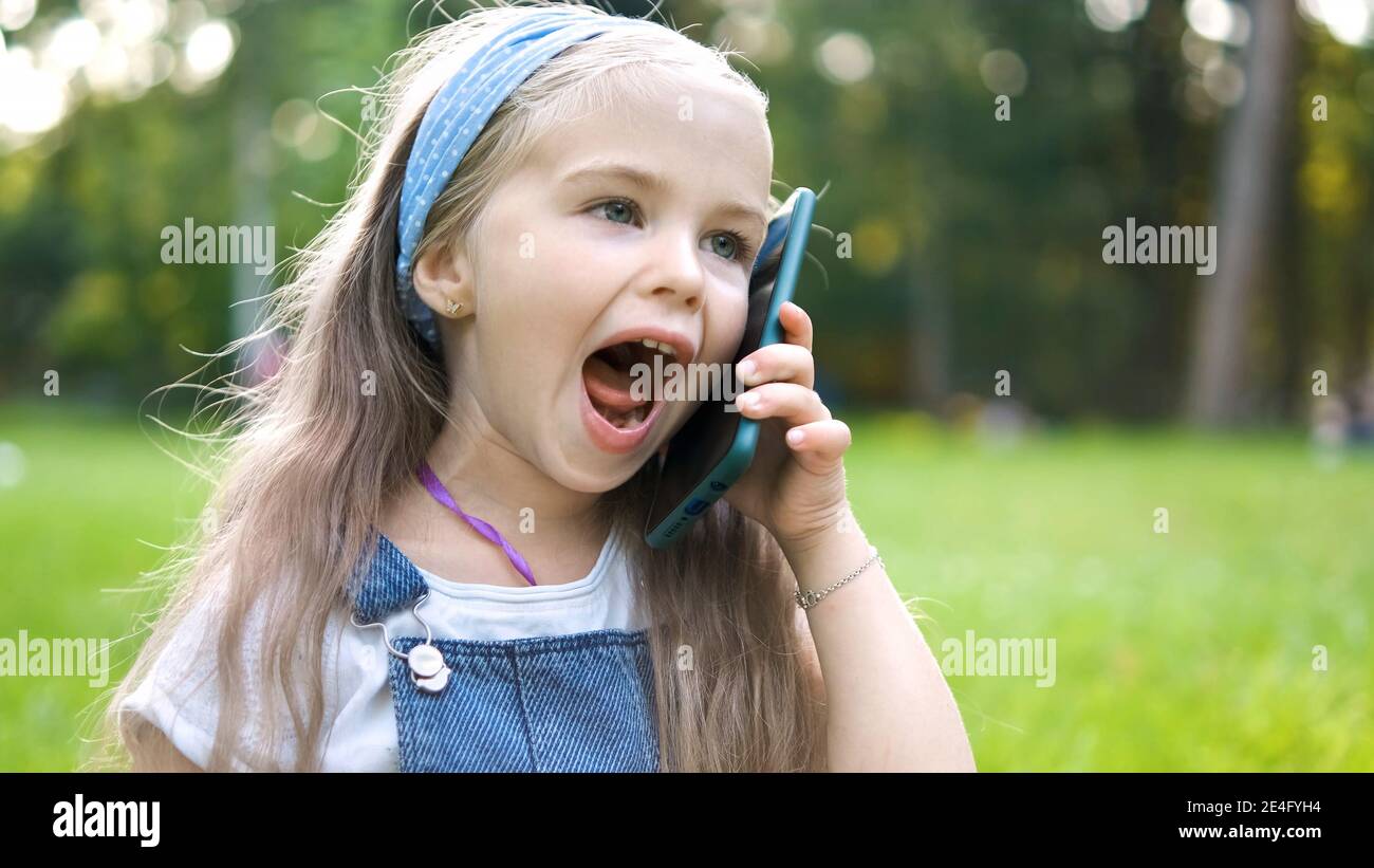 Positive little child girl having conversation on her mobile phone in ...