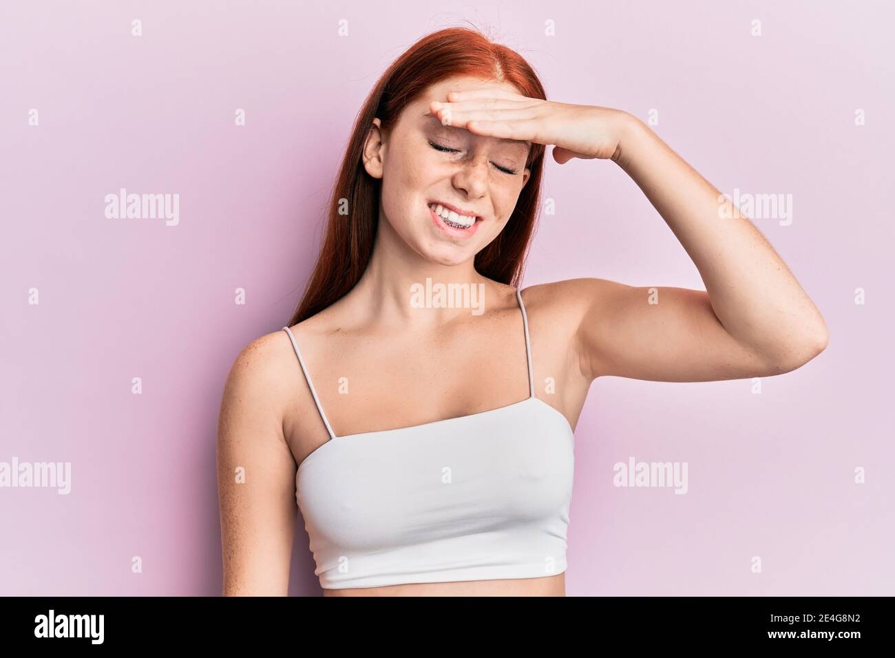 Young red head girl standing over pink background stressed and ...