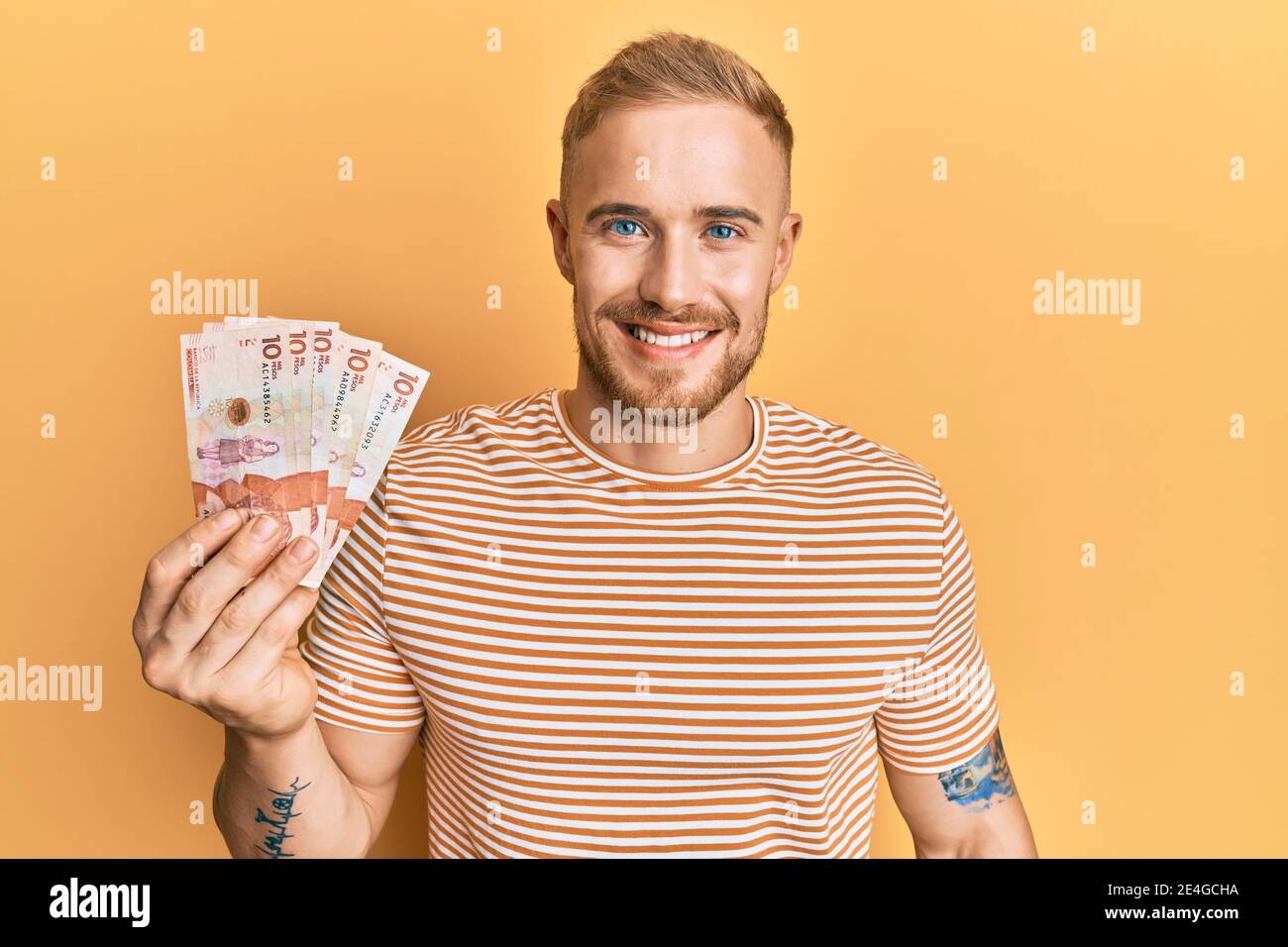 Young caucasian man holding 10 colombian pesos banknotes looking ...