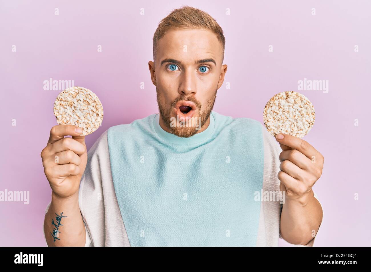Young caucasian man eating healthy rice crackers afraid and shocked ...
