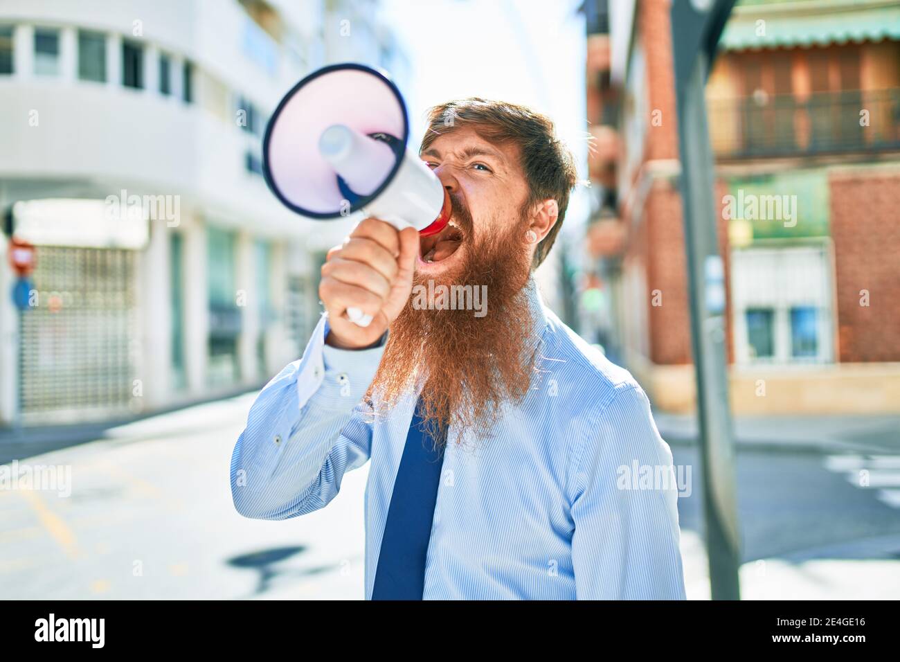 Young redhead businessman with angry expression. Screaming using ...