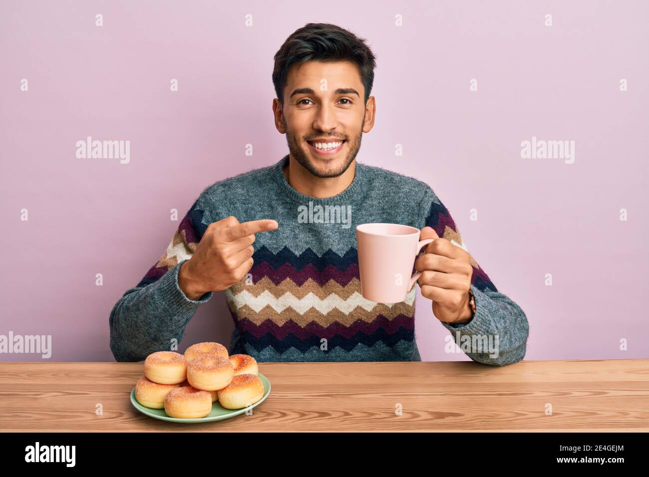 Young handsome man eating doughnuts and drinking coffee smiling happy ...