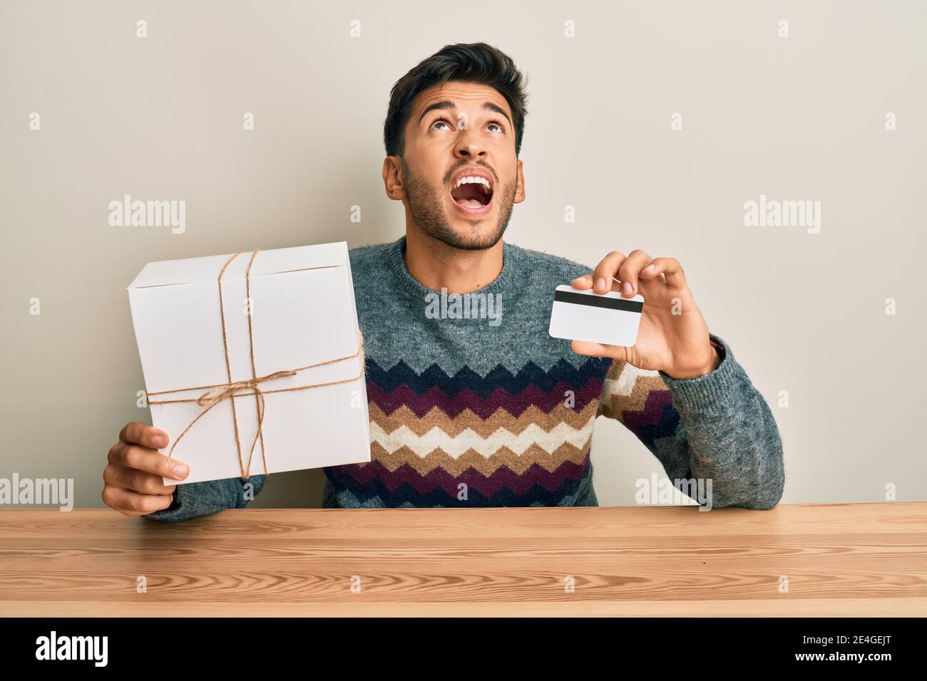 Young handsome man holding gift and credit card angry and mad screaming ...