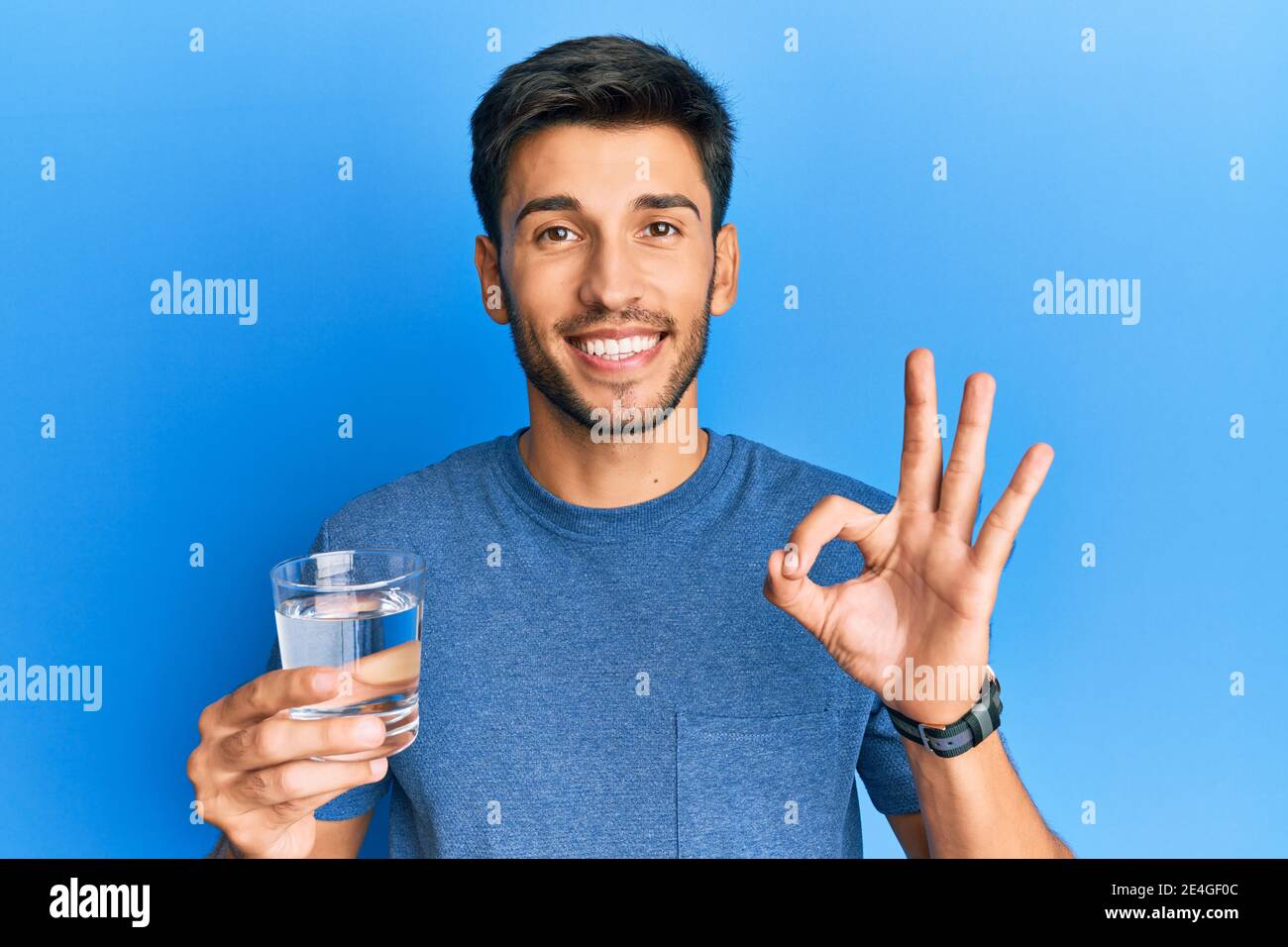 Young handsome man drinking glass of water doing ok sign with fingers ...
