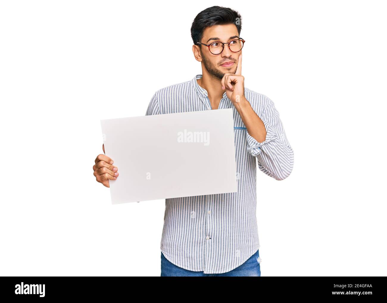Young handsome man holding blank empty banner serious face thinking ...