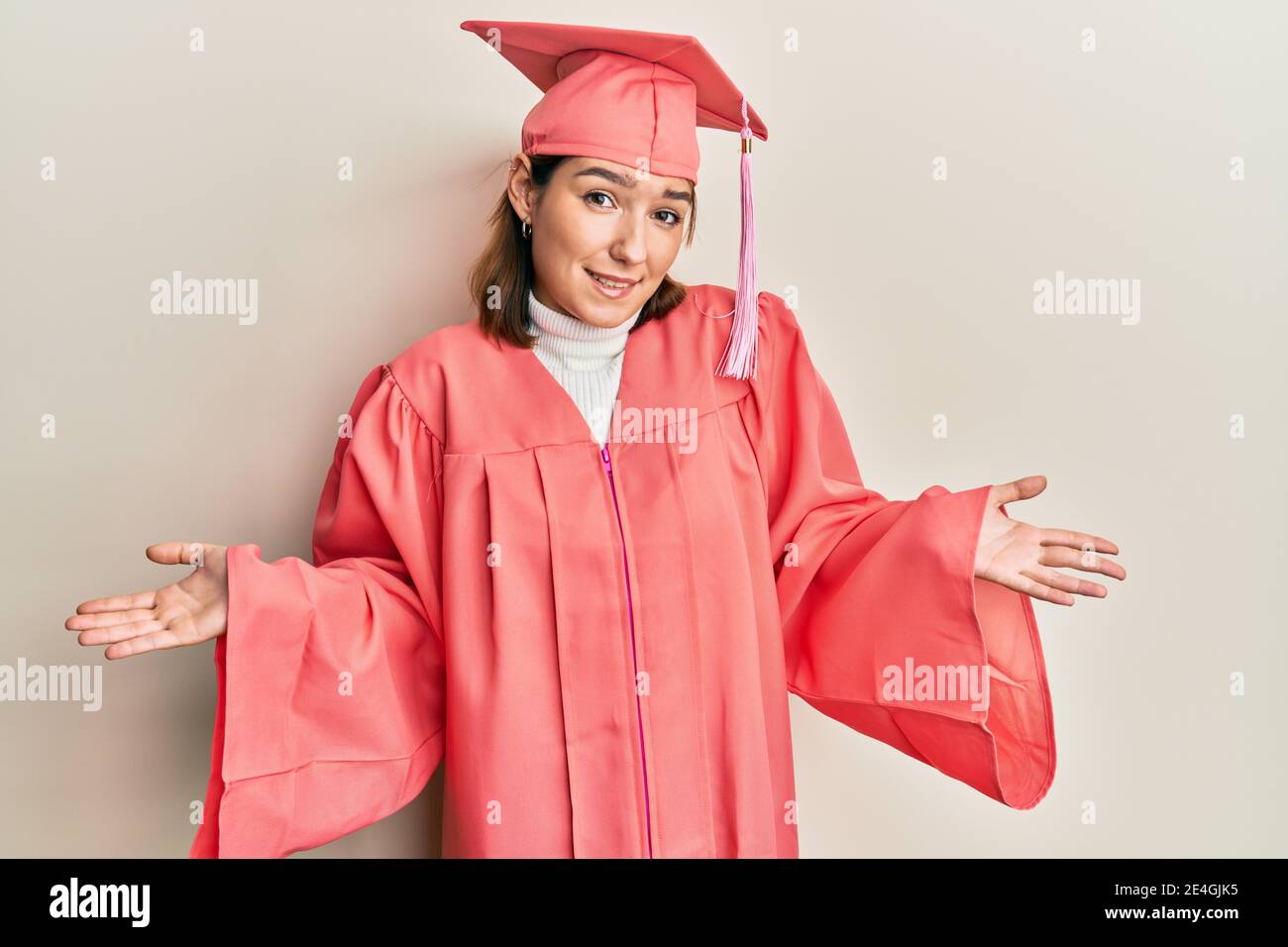 Young caucasian woman wearing graduation cap and ceremony robe clueless ...