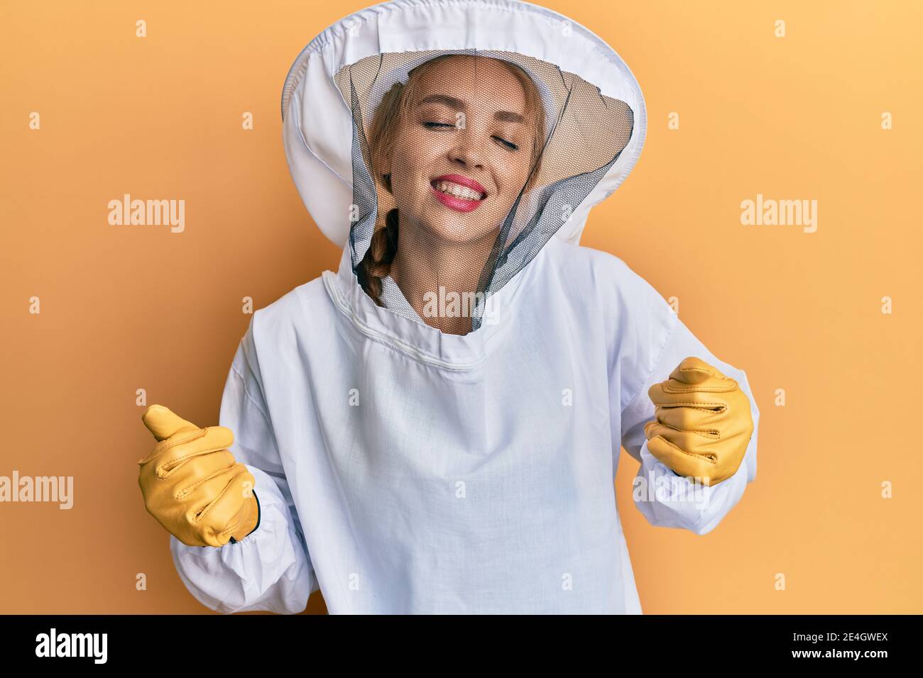 Beautiful blonde caucasian woman wearing protective beekeeper uniform very happy and excited ...