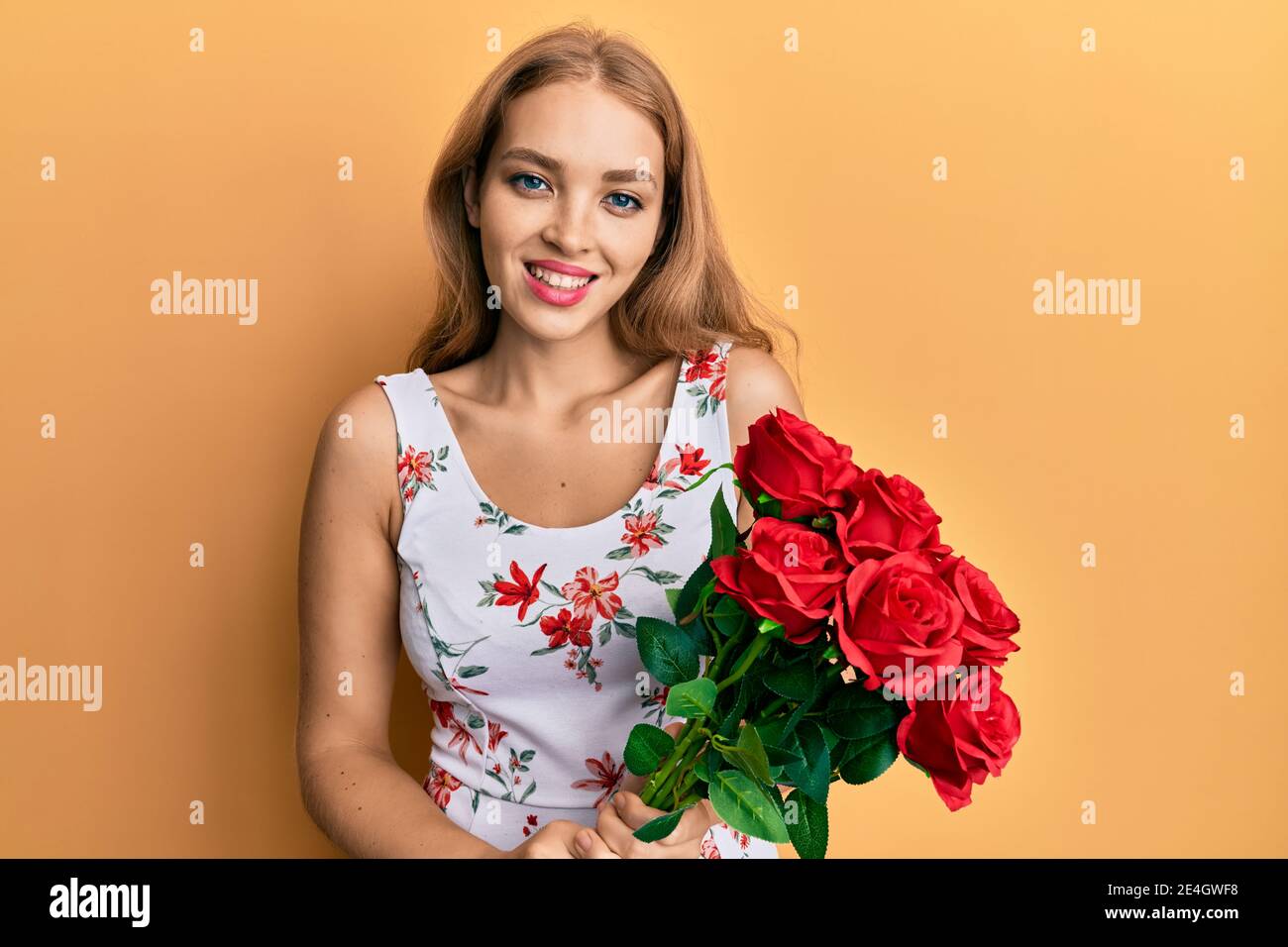 Beautiful blonde caucasian woman holding bouquet of red roses looking ...