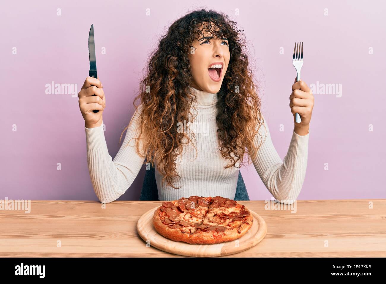 Young hispanic girl eating tasty pepperoni pizza angry and mad ...
