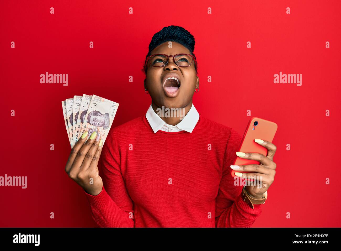 Young african american woman using smartphone holding mexican peso ...