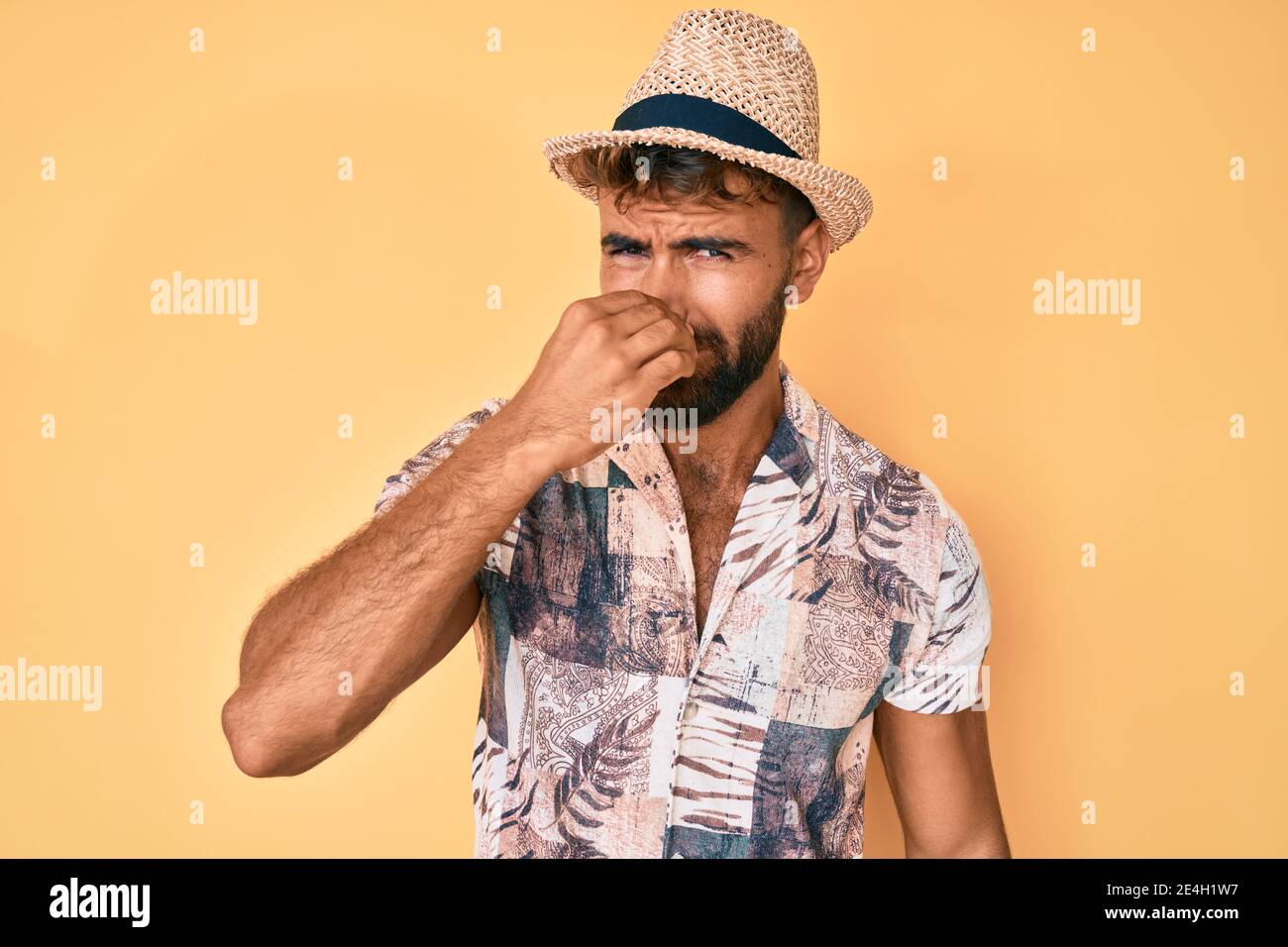 Young hispanic man wearing summer hat smelling something stinky and ...