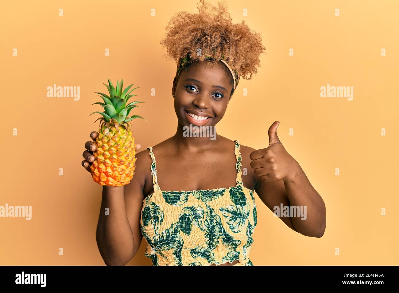 Young african woman with afro hair holding pineapple smiling happy and ...