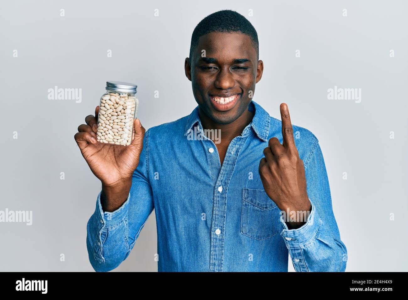 Young african american man holding jar of beans smiling with an idea or ...