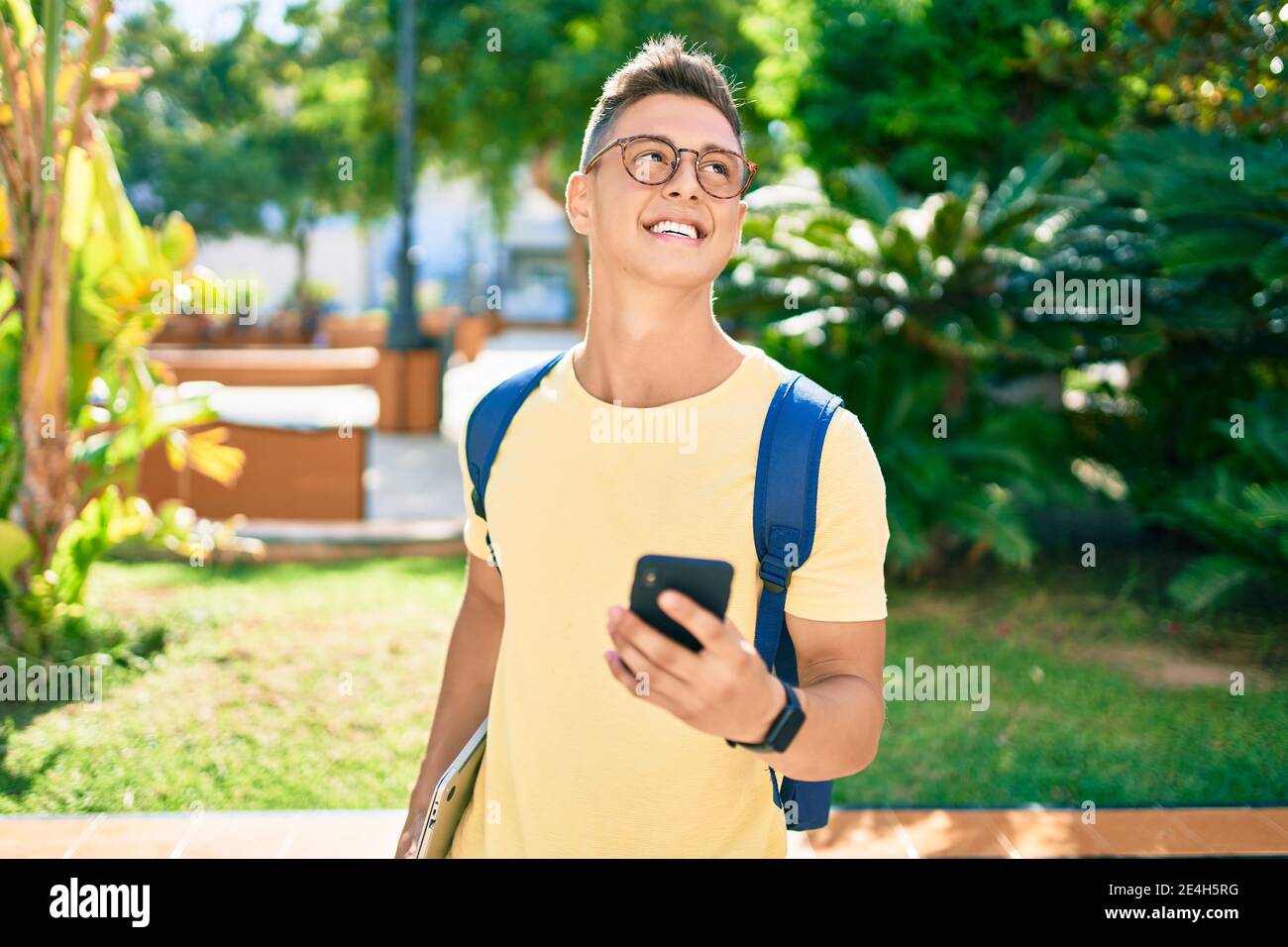 Young hispanic student smiling happy using smartphone walking the ...