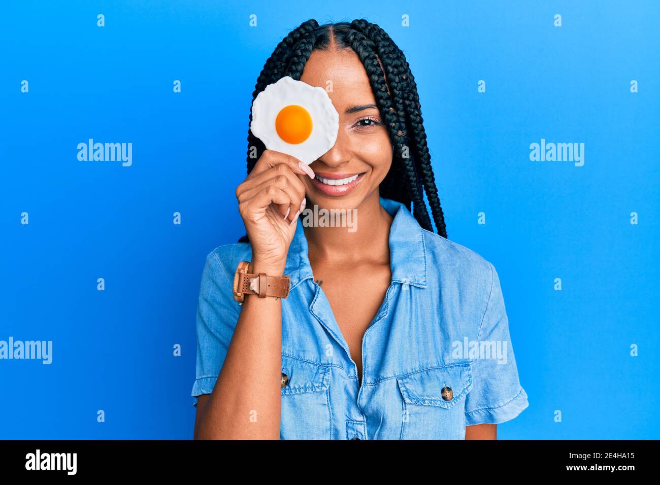 Beautiful hispanic woman holding fried egg looking positive and happy ...